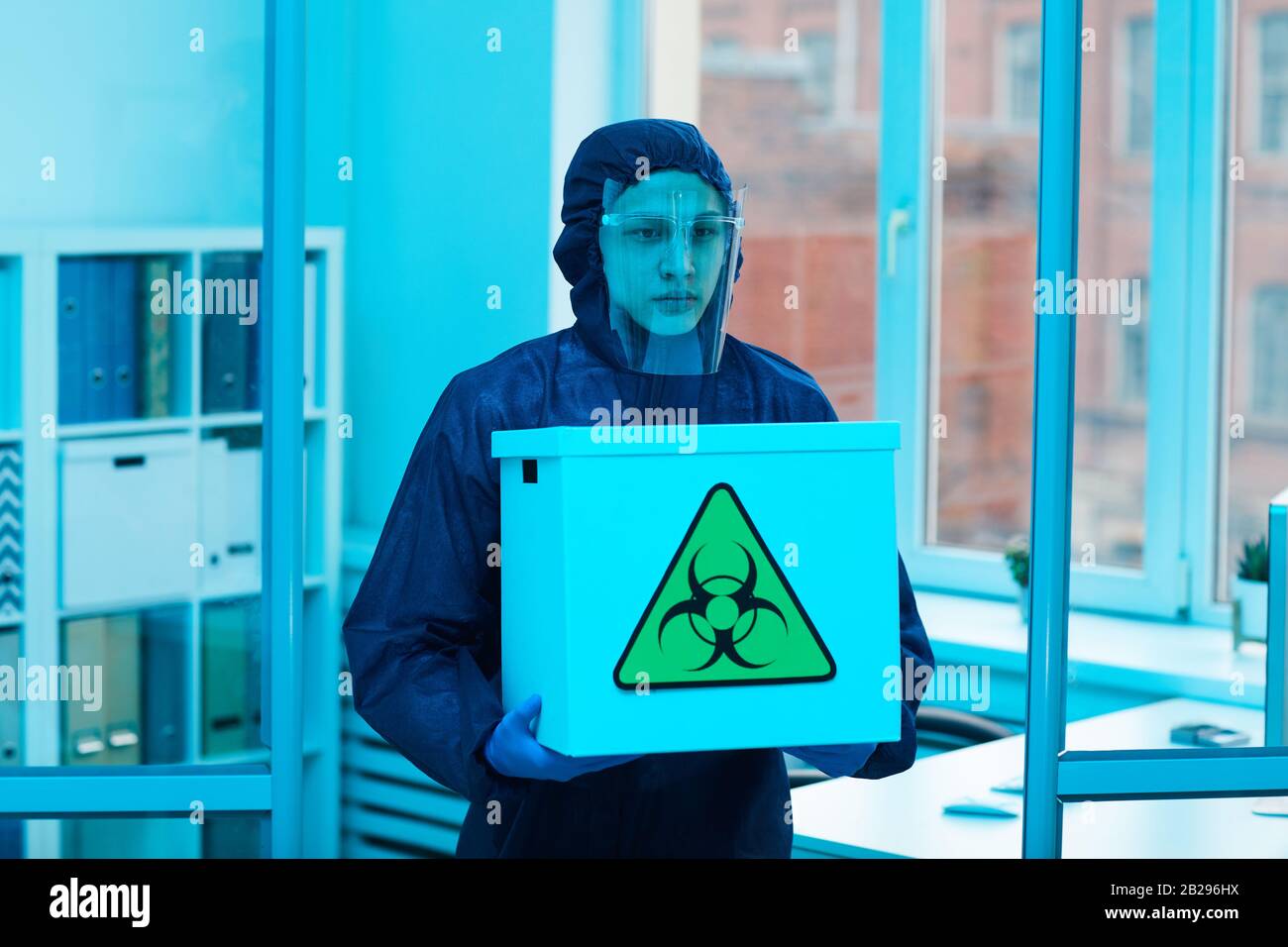 Waist up portrait of male scientist wearing biohazard gear holding box ...