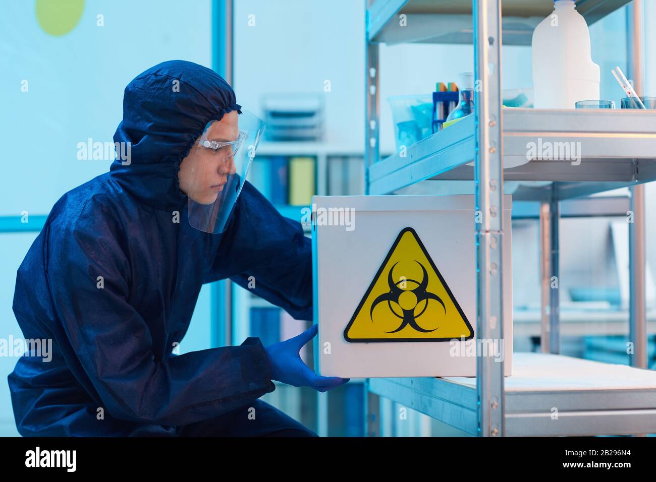 Side view portrait of male scientist wearing biohazard gear holding box ...