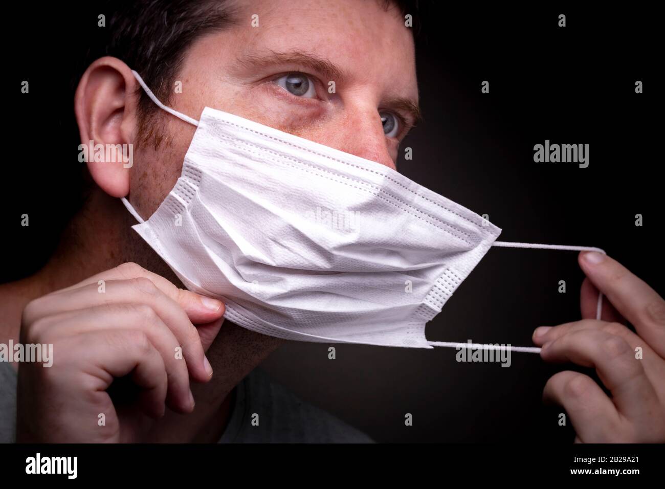 Caucasian male putting on a face mask with one hand stretching the ...