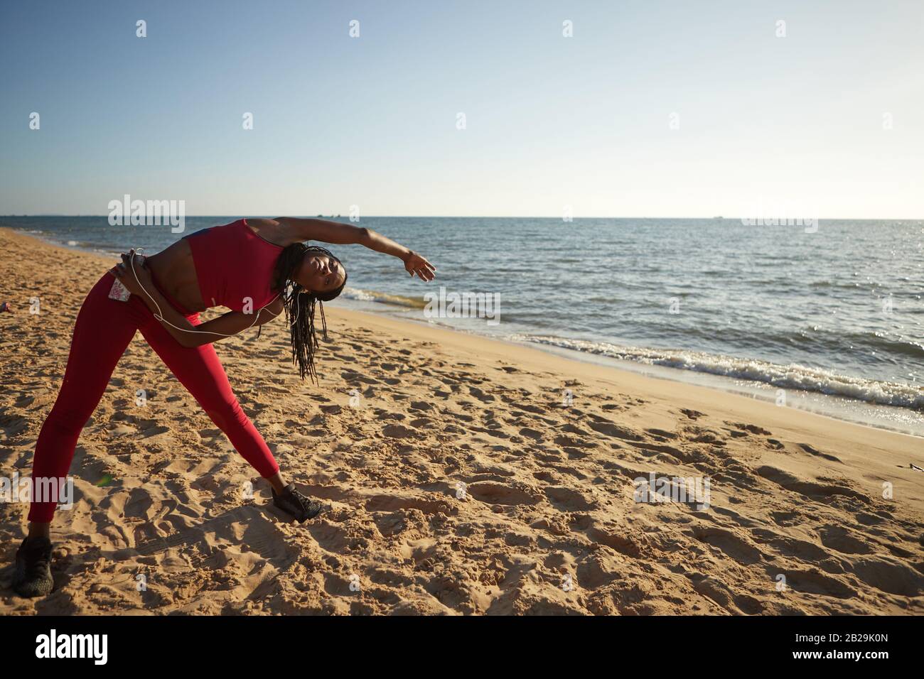 Flexible fit woman standing on sandy beach and bending to her left ...
