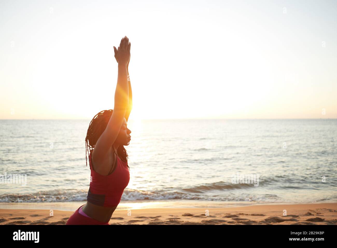 Fit young woman standing in morning sun rays and practicing warrior ...