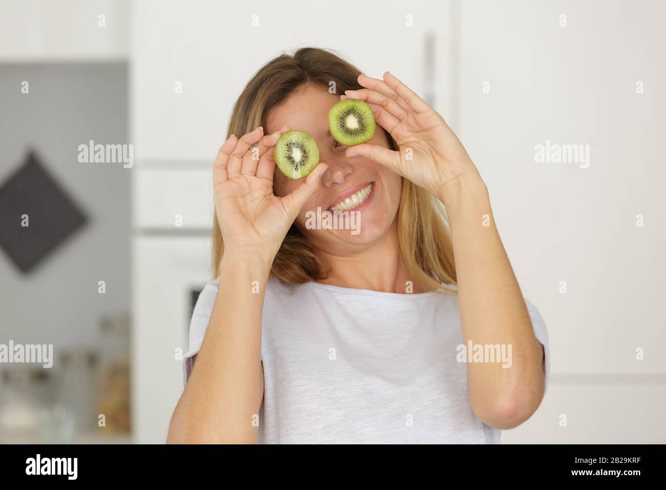 beautiful young woman holding two kiwis on her eyes Stock Photo - Alamy