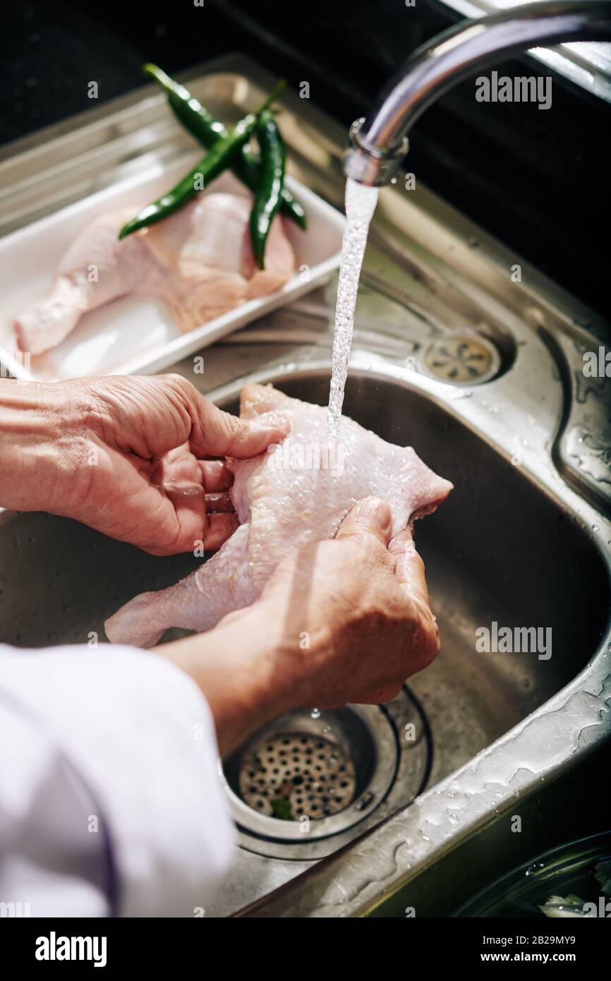 Hands of senior person rinsing chicken thights under cold water from ...