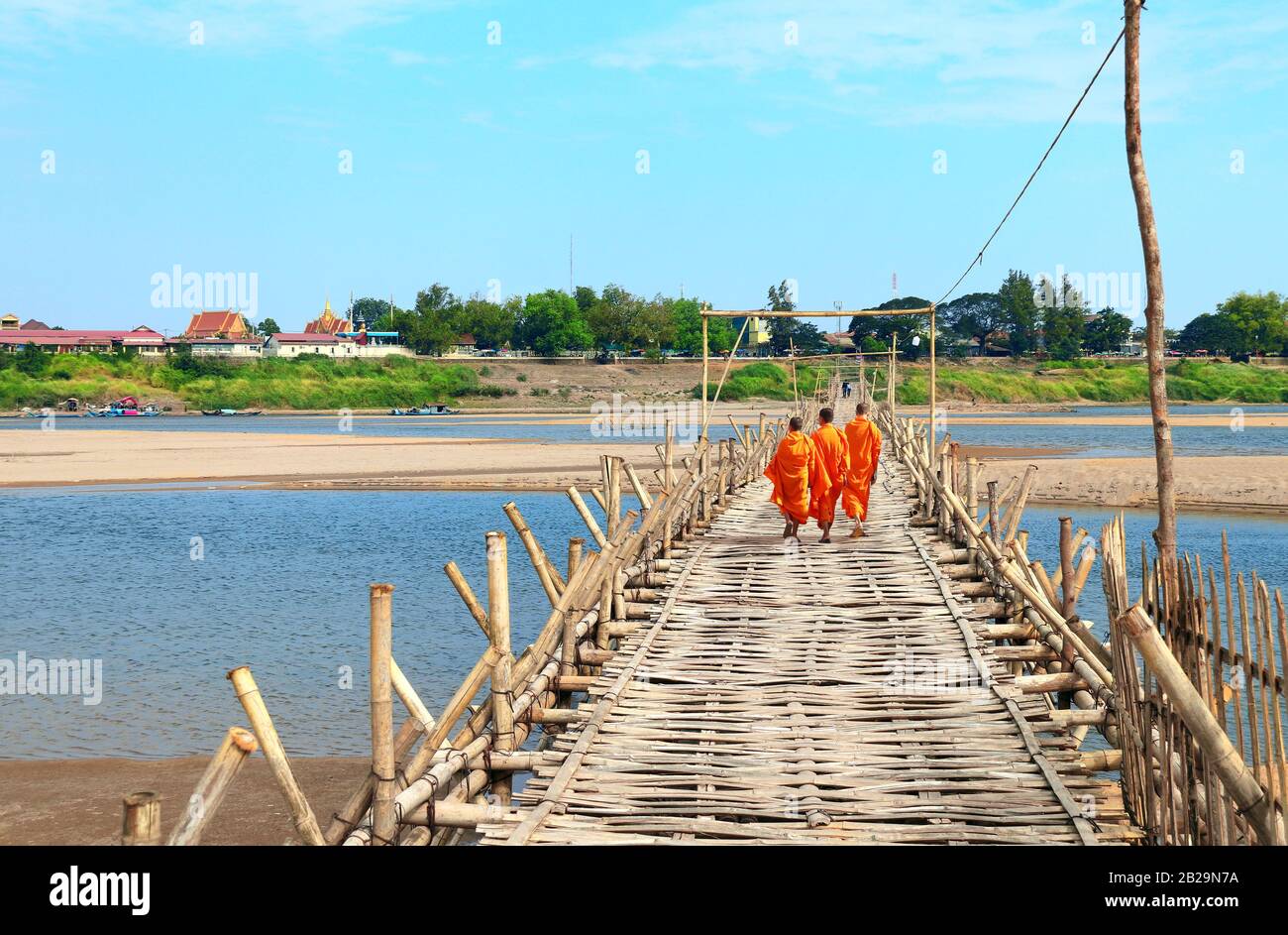 Three buddhist monks on bamboo bridge across Mekong river between ...