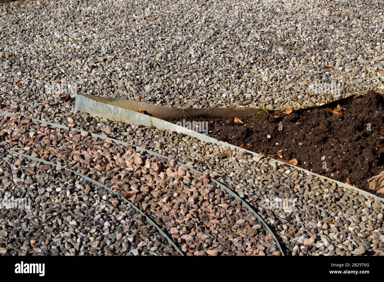 Metal edging separating dirt and different colors of gravel in a park ...