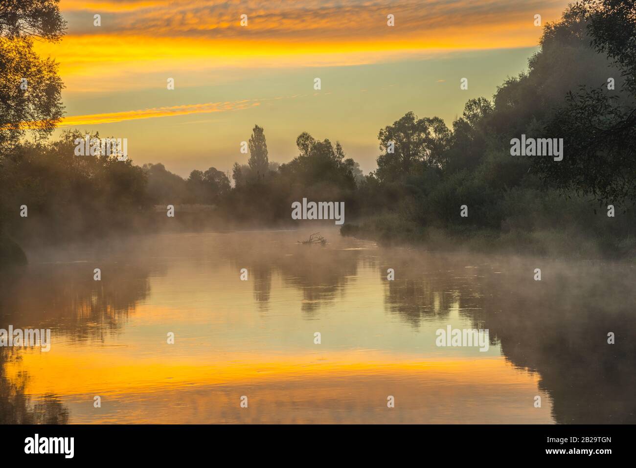 Morning mist swirls over river. Sunrise orange clouds reflect in ...