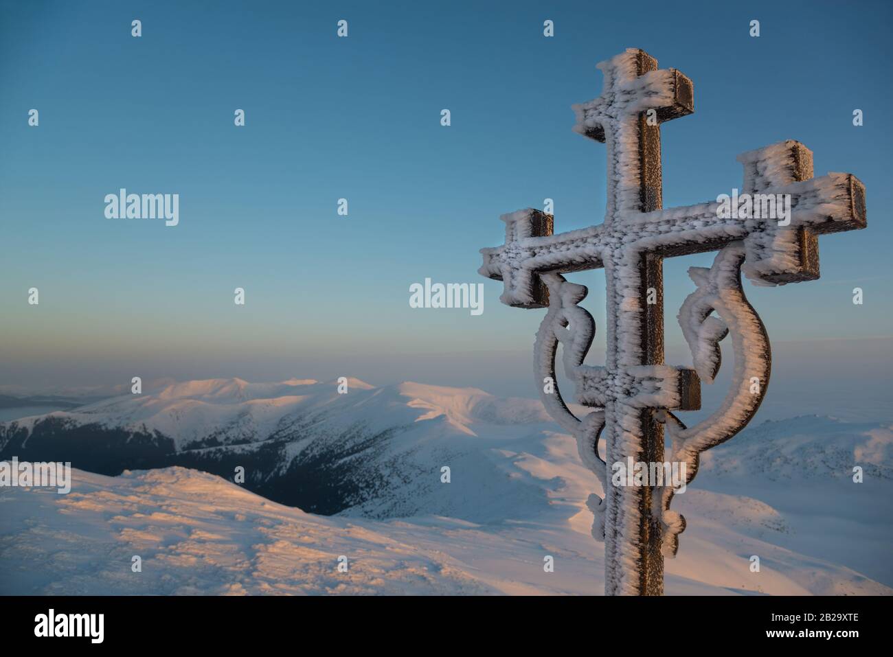 Frosted cross against beautiful sunrise scene in mountains. White snowy ...