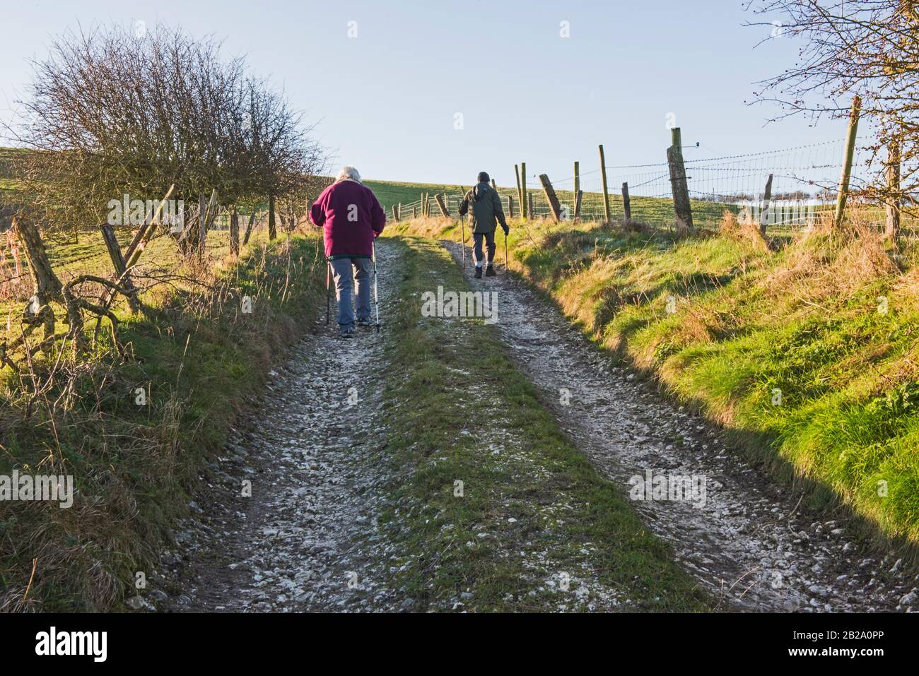 Two elderly people walking ramblers on remote country lane road up a ...