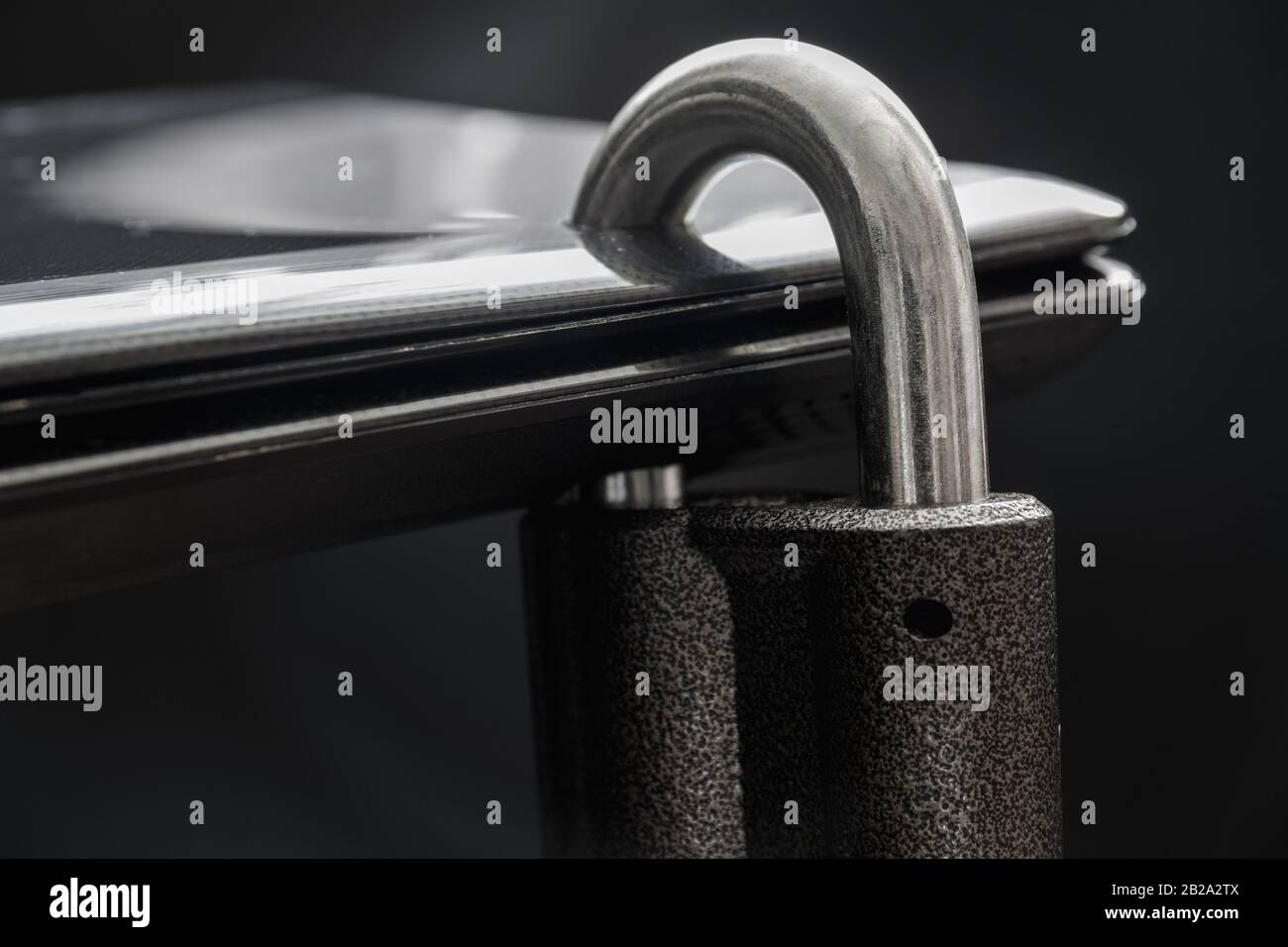 Locked steel padlock in a drilled hole of the black laptop on dark ...