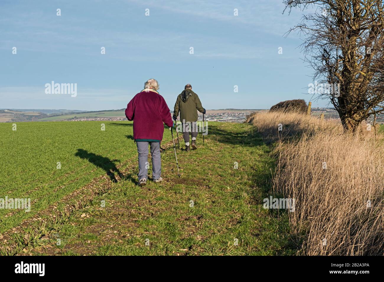 Two elderly people walking ramblers on remote country lane road up a ...