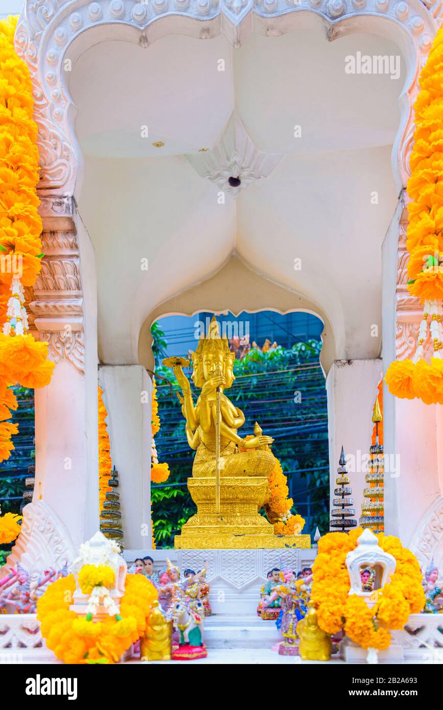 Golden multi-faced buddha statue in a shrine with orange flowers ...
