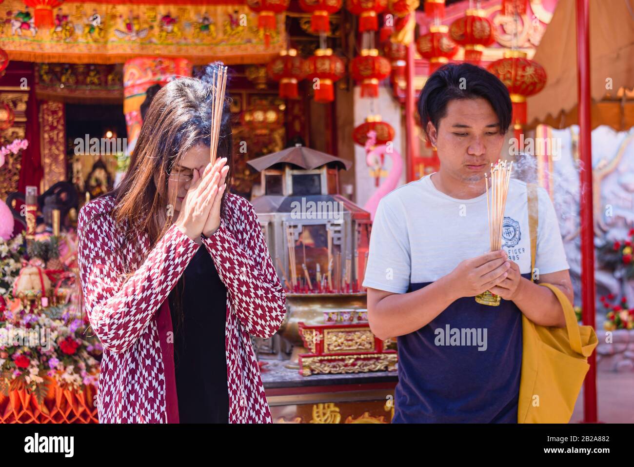 A man and woman hold incense sticks while they pray at a Chinese Temple ...