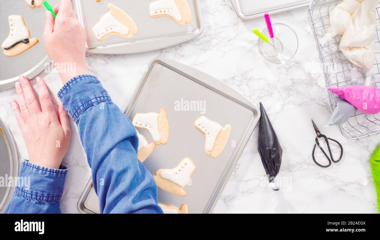 Flat lay. Decorating ice skate shaped sugar cookies with black color ...