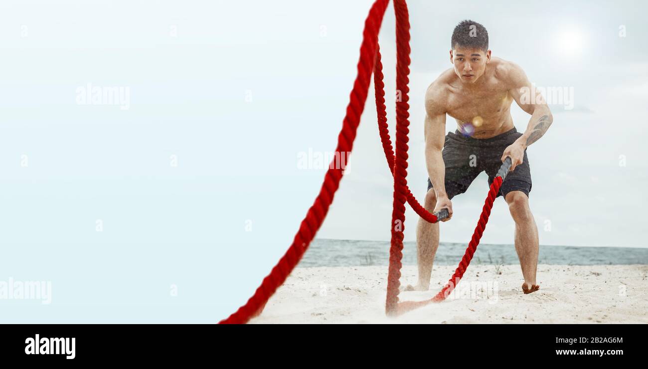 Young healthy man, athlete doing exercise with the ropes at the beach ...