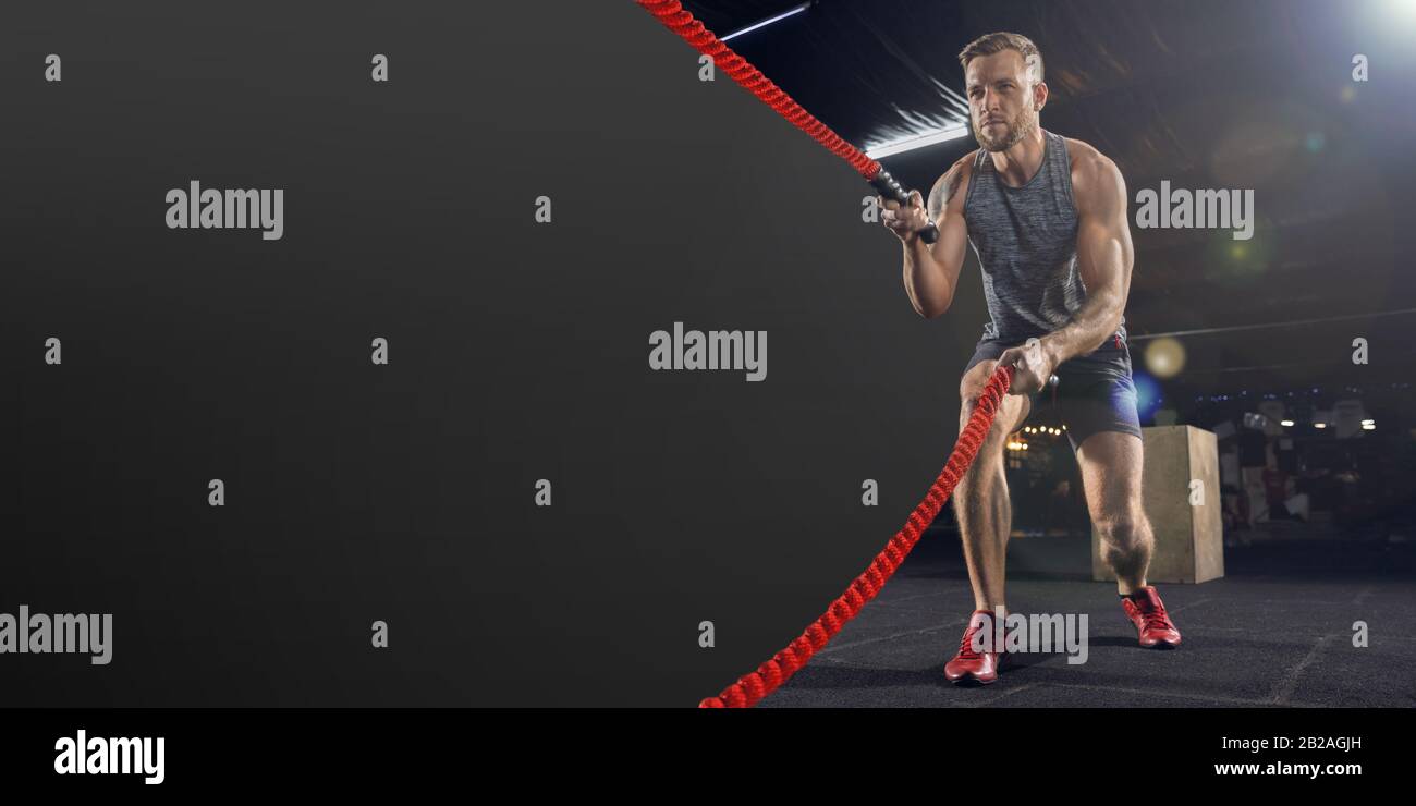 Young healthy man, athlete doing exercise with the ropes in the gym ...
