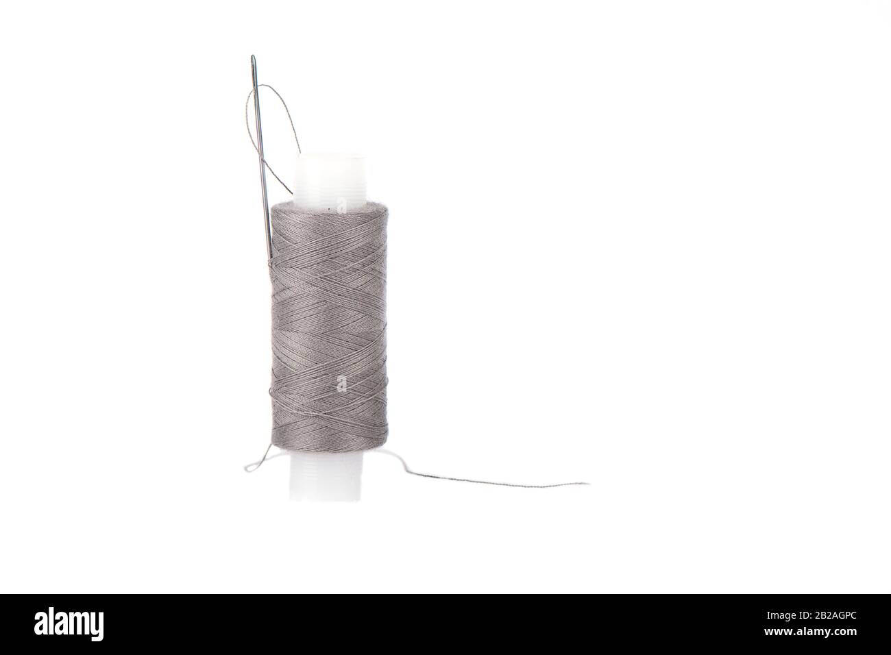 Close-up photo of a spool with grey thread and a needle isolated over ...