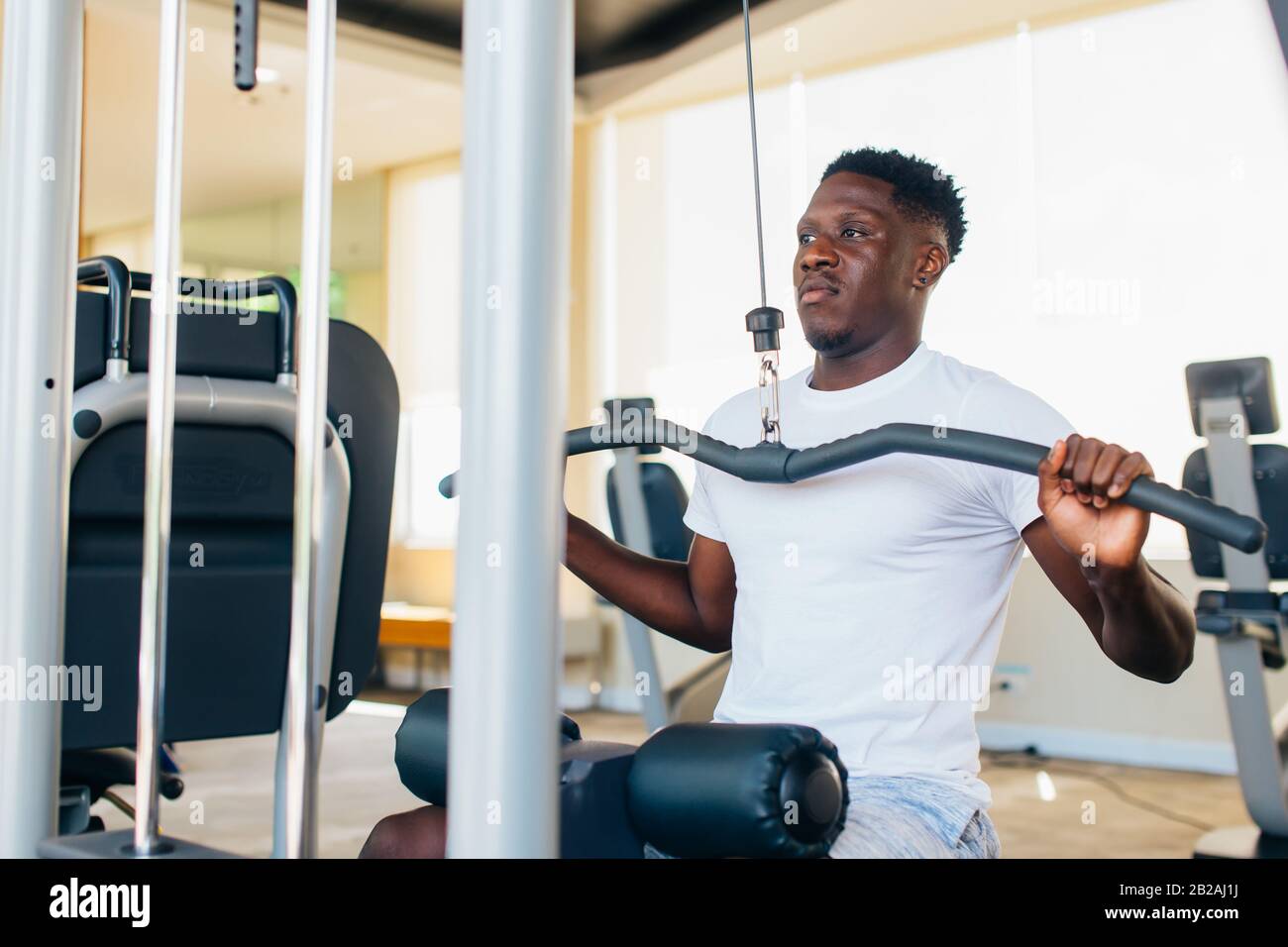 Strong African American man in sportswear pulling cable with bar while ...