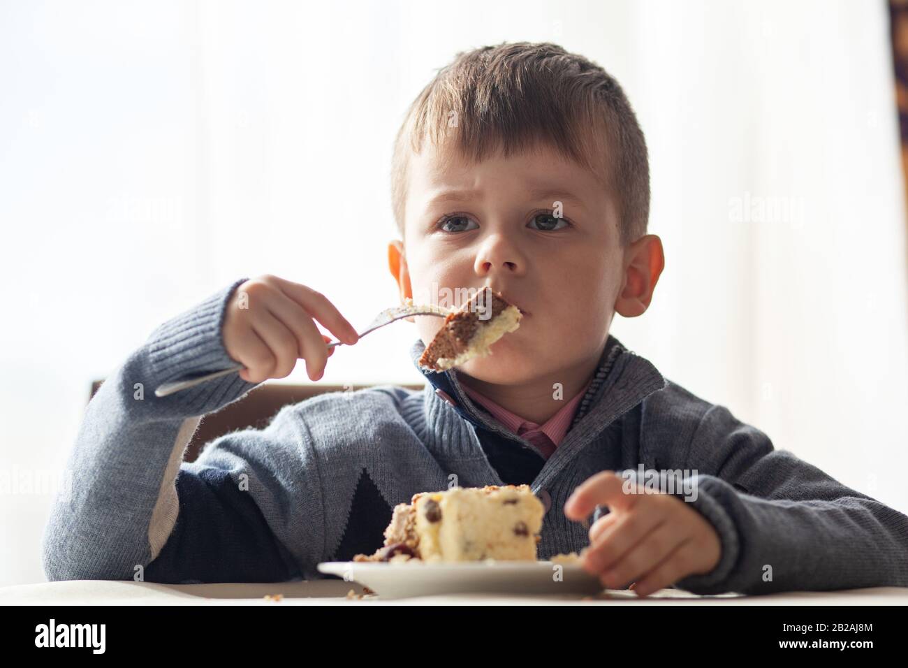 Cute little boy in cafe eat a big piece of cake with a fork. Desserts ...