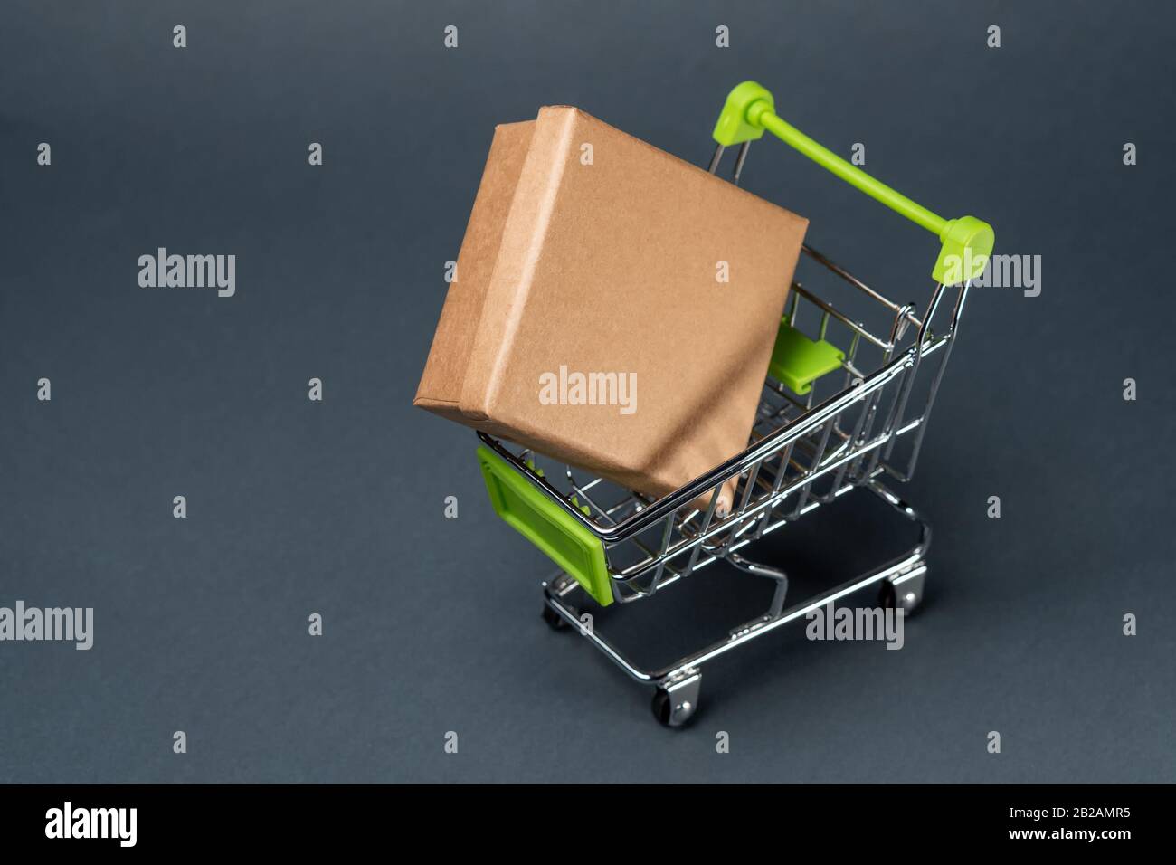 cardboard box in a toy shopping trolley on a gray background. Copy ...