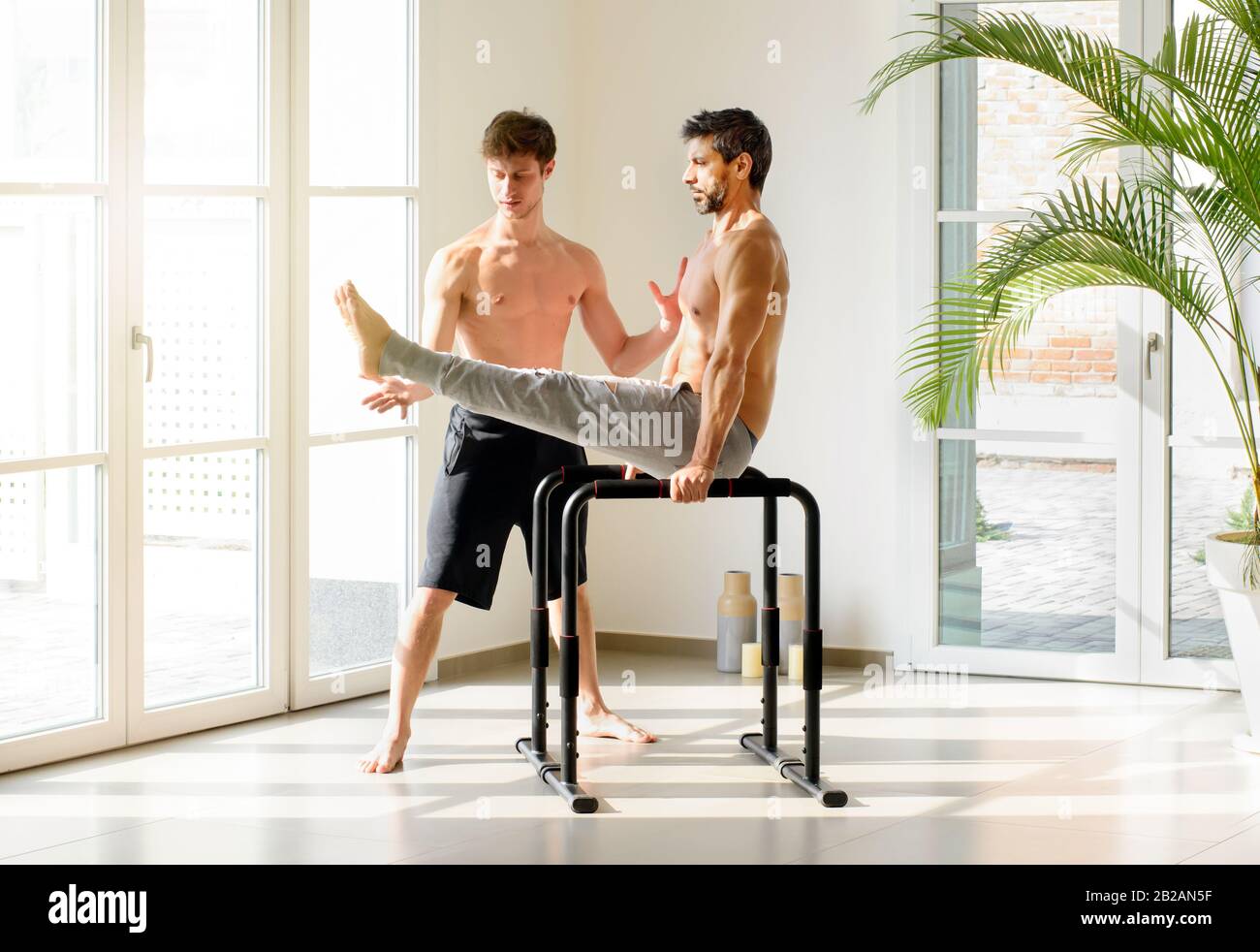 Two athletic men working out doing calisthenics with one assisting the ...
