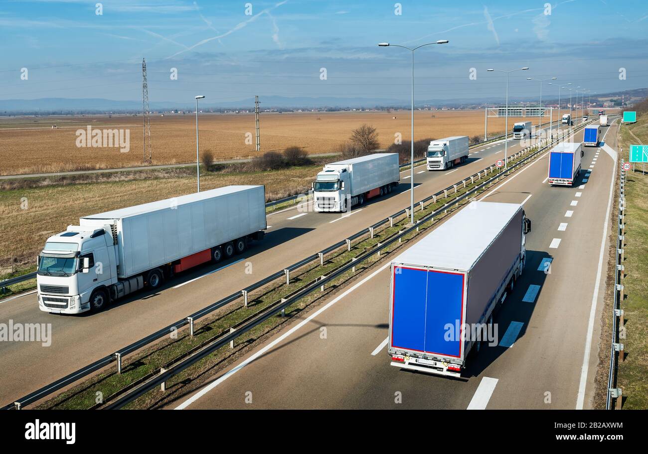 Convoy of transportation trucks passing on a highway on a bright blue ...