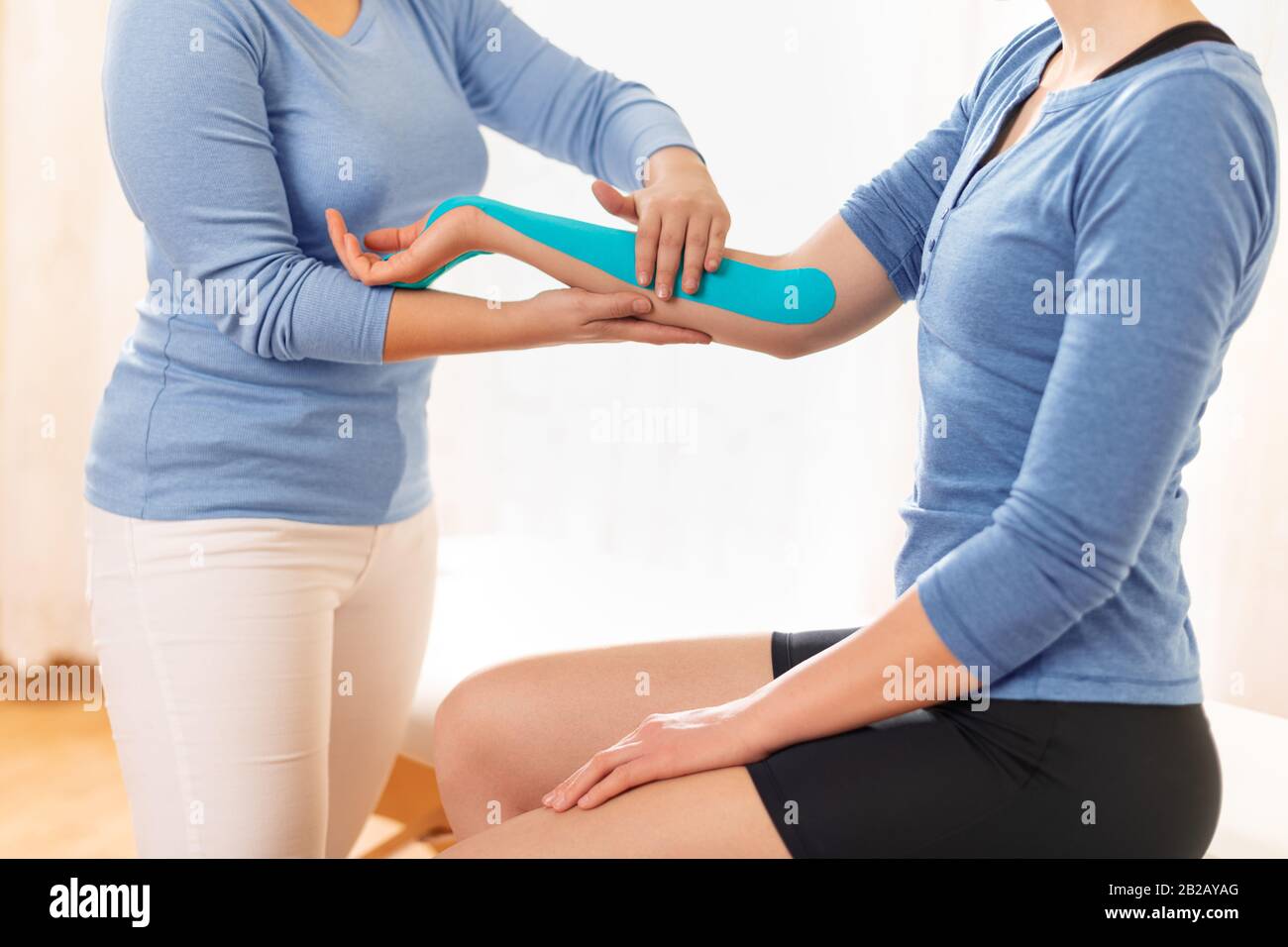 Female physiotherapist applying kinesio tape on patient's arm. Kinesiology, physical therapy ...