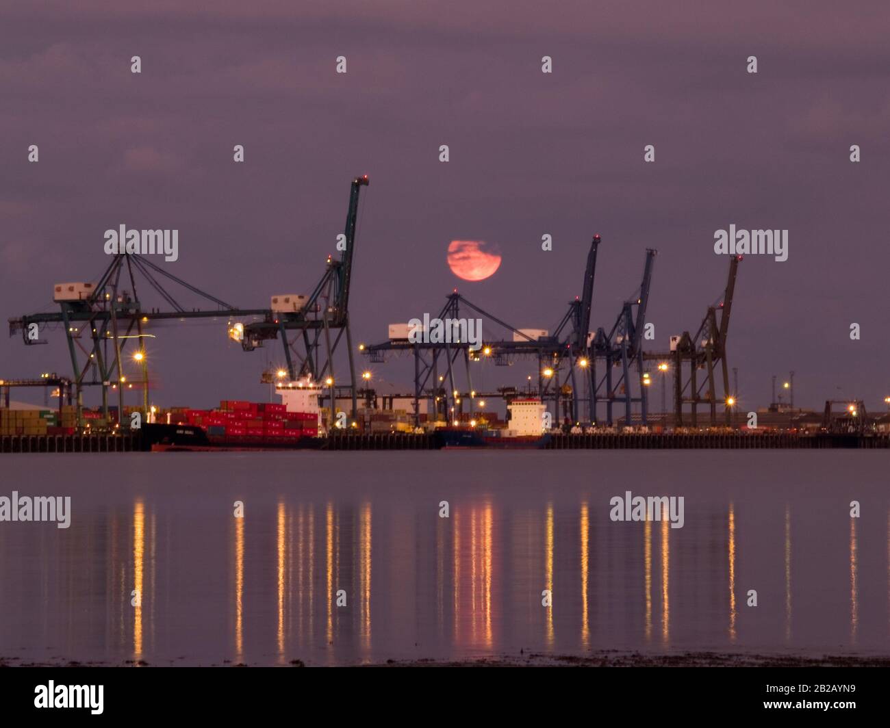 Containers Ships being loaded and unloaded at night under a big moon at ...
