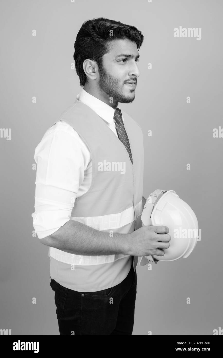 Young handsome Indian man construction worker against gray background ...