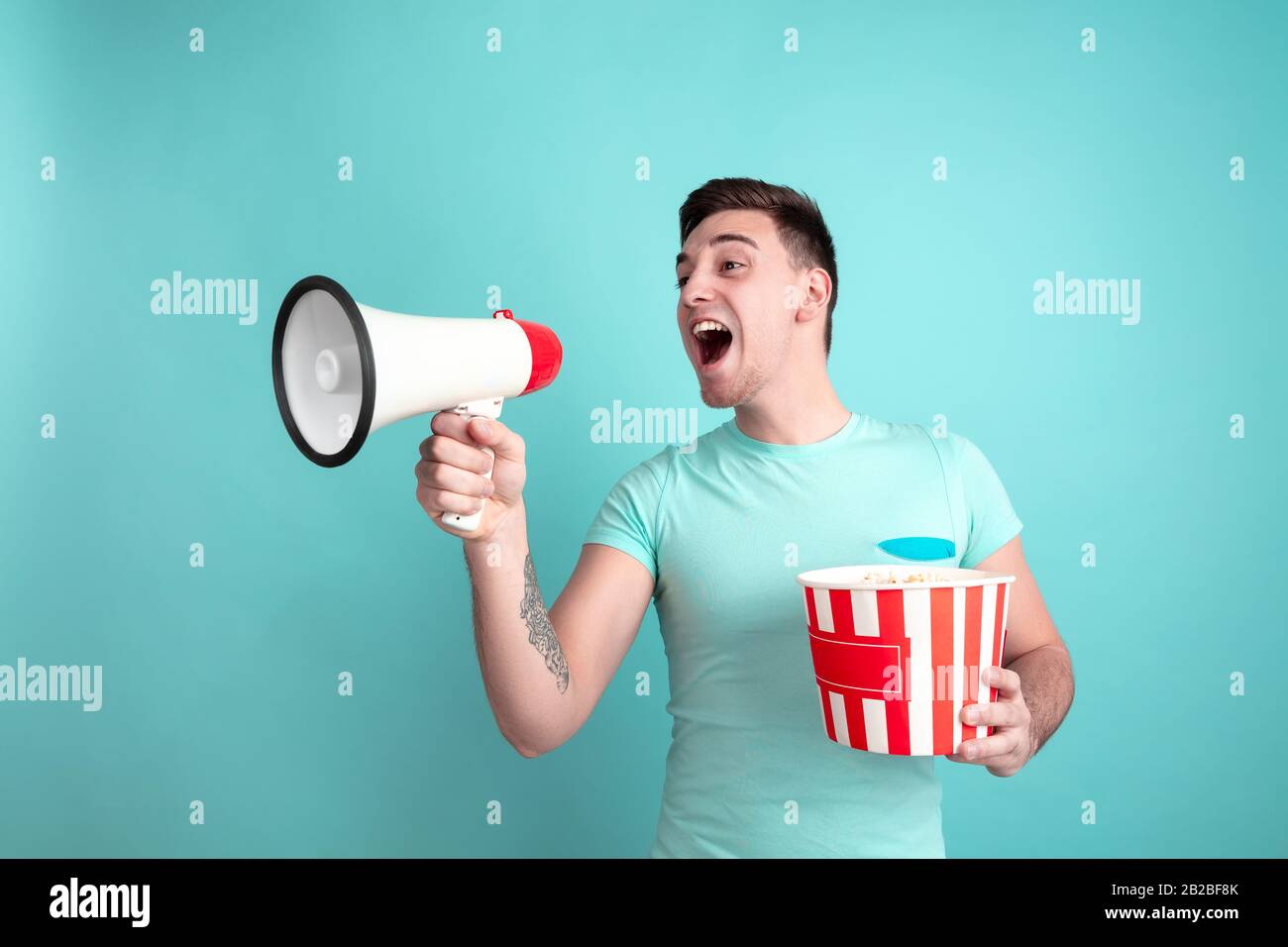 Shouting with popcorn. Caucasian young man's portrait isolated on blue ...