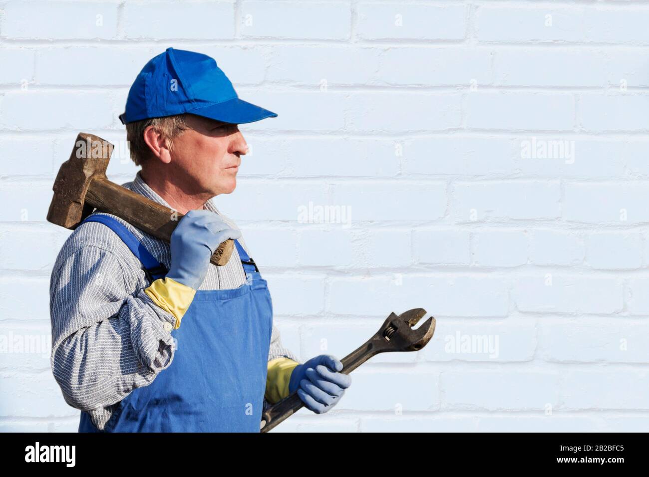 worker in blue overalls with a sledgehammer and a wrench. Serious look ...