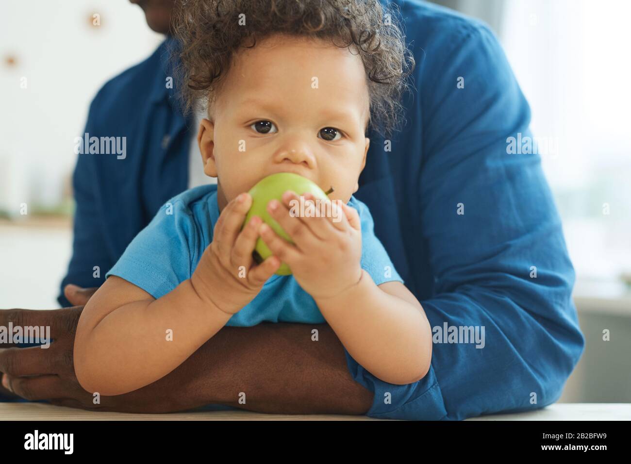 Portrait of cute African-American toddler eating apple and looking at ...