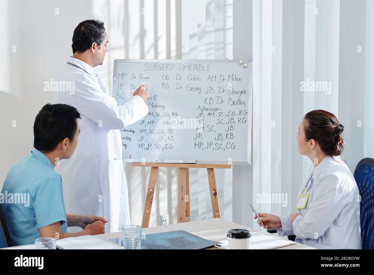 Chief doctor discussing surgery timetable on whiteboard with colleagues ...
