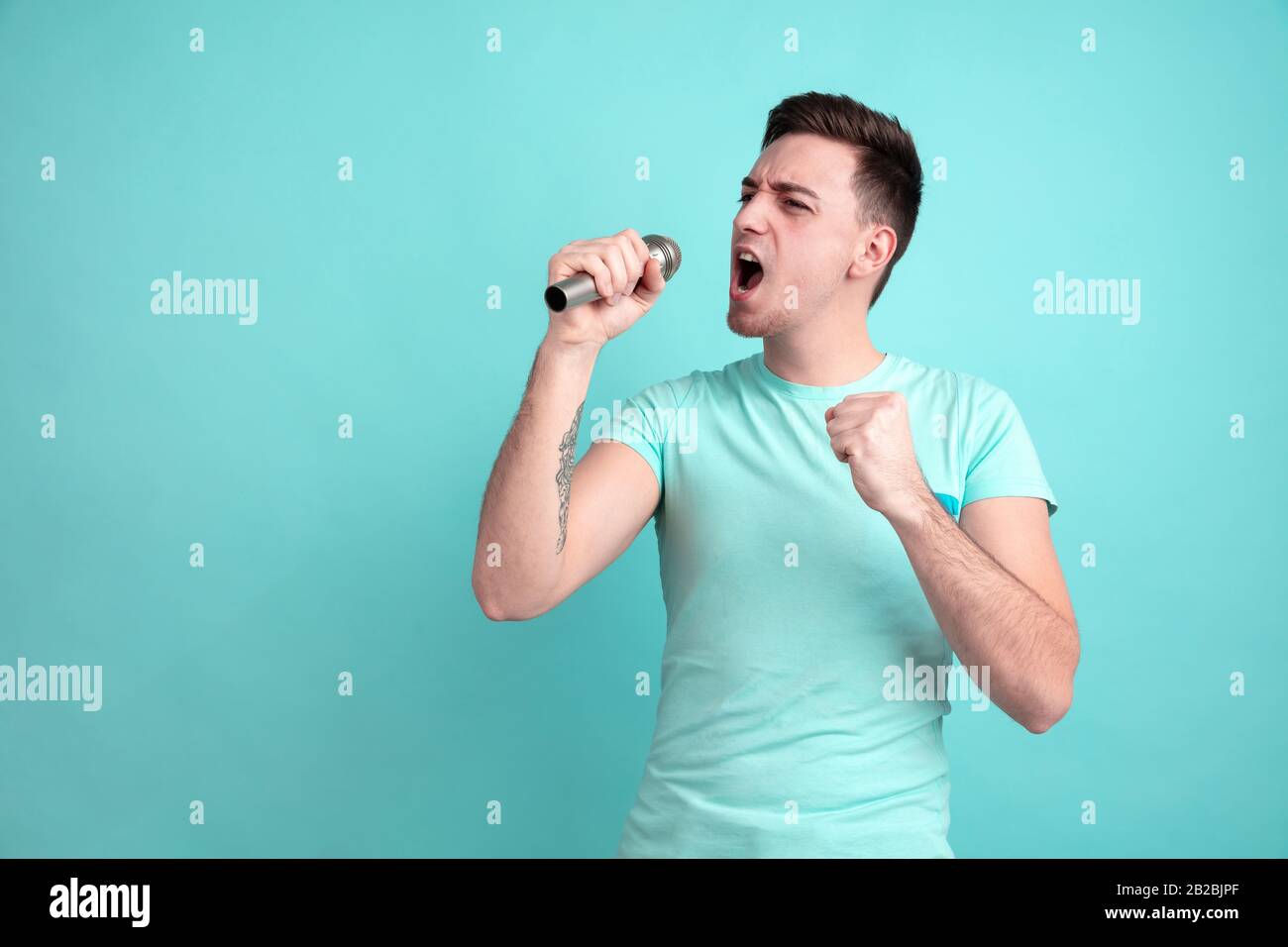 Singing like a star. Caucasian young man's portrait isolated on blue ...