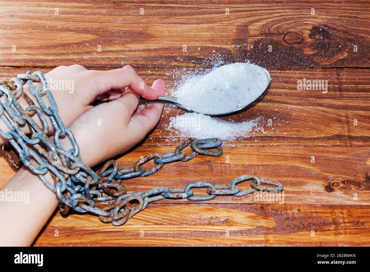 Sea salt in spoon on wooden background. Hands chained in a chain ...