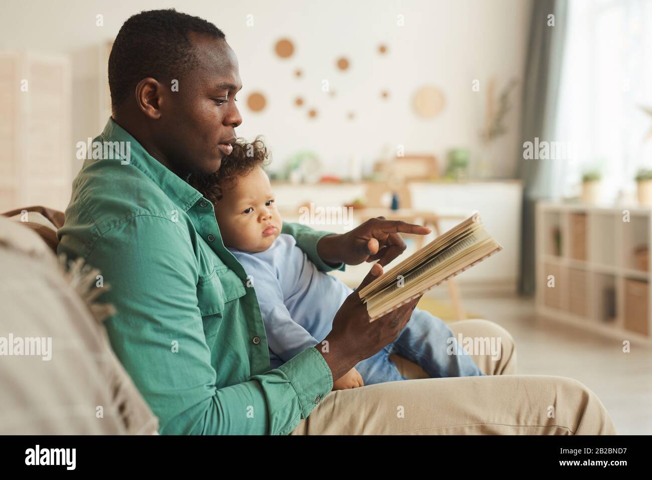 Side view portrait of caring African-American dad reading book to cute ...
