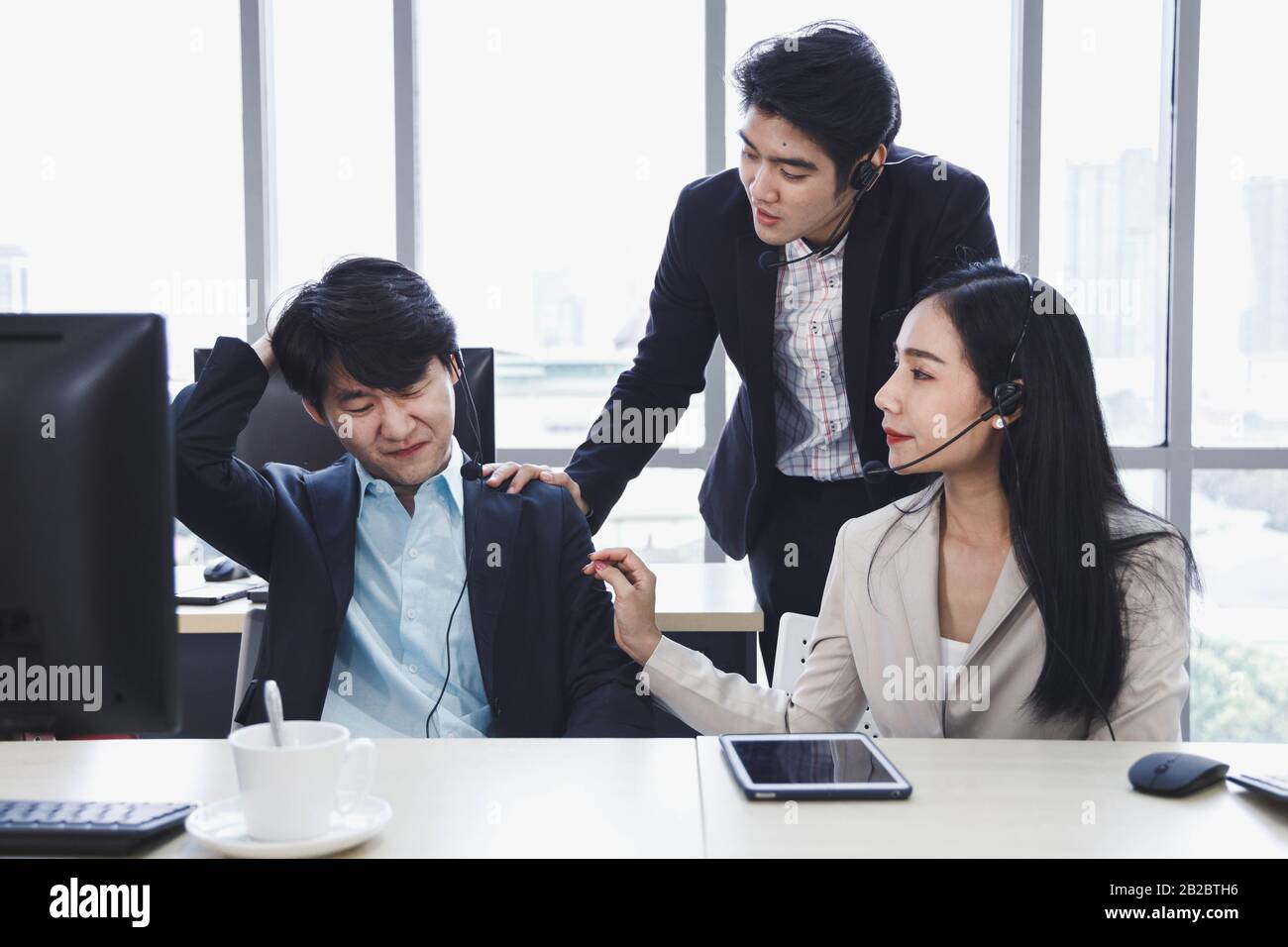 Two Asian call center agents cheer their colleague up who has problem ...