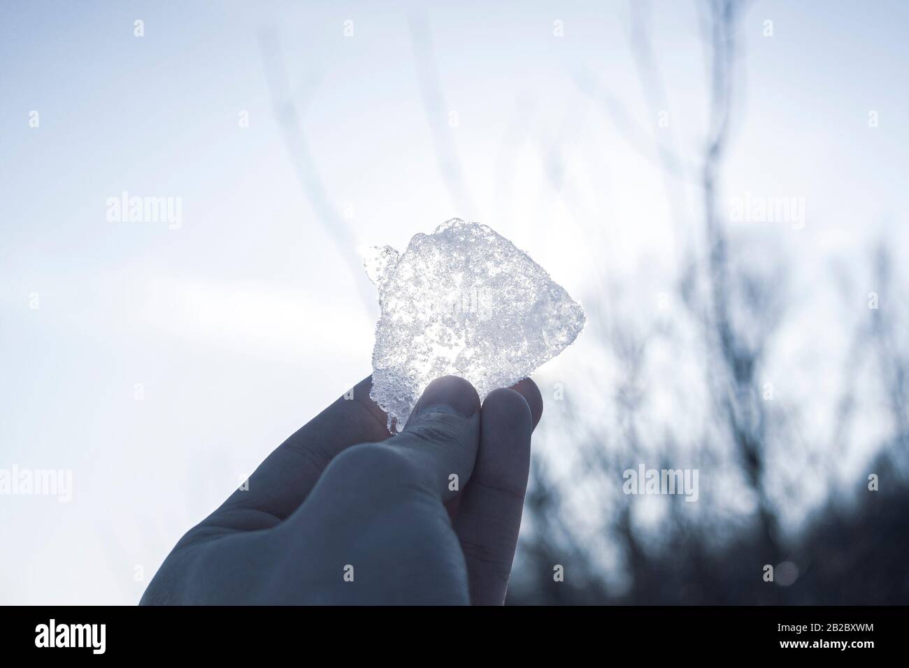 Piece of ice in man's hand close up against the sun. Look at the sun ...