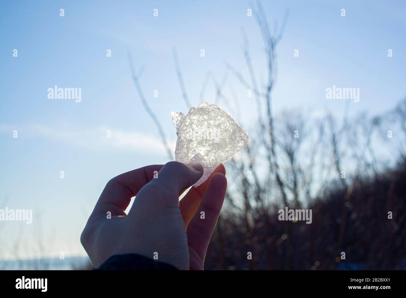 Piece of ice in man's hand close up against the sun. Look at the sun ...