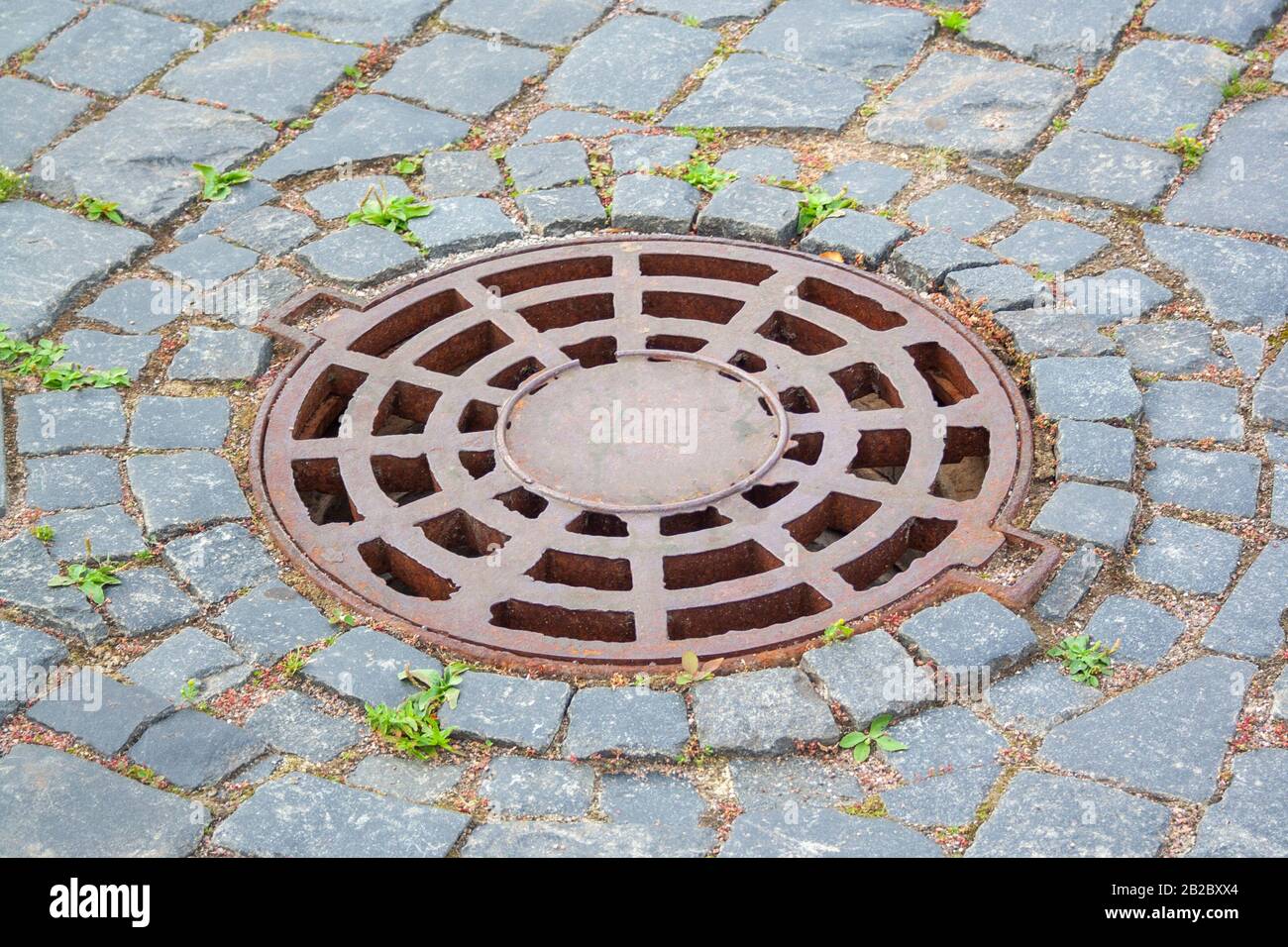 Manhole cover near paving stones. Rusty manhole cover on the walkside ...