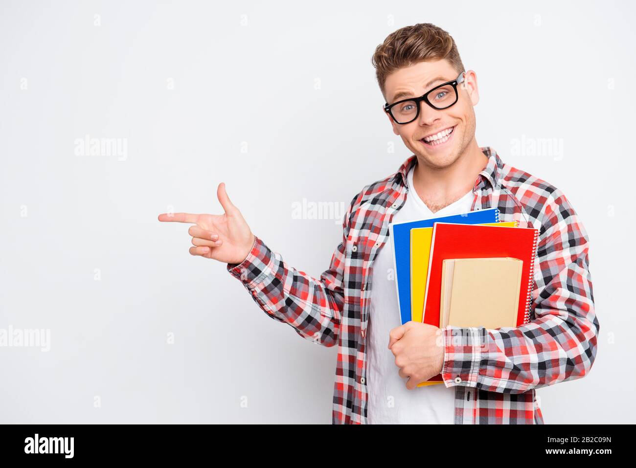Young smart happy student with books pointing on copy space Stock Photo ...