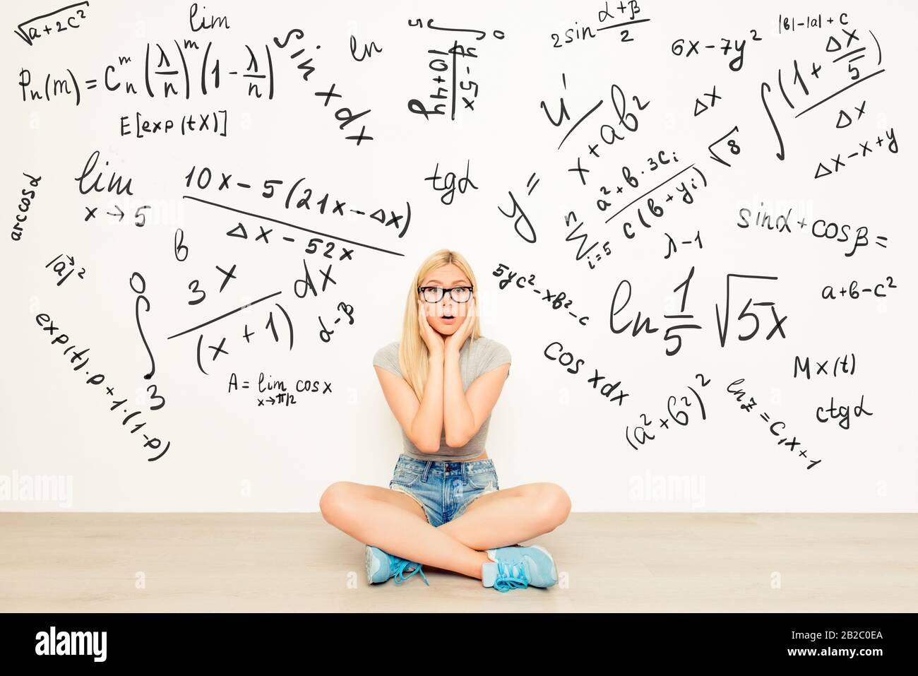 attractive shocked girl in spectacles sitting on floor near wall with ...