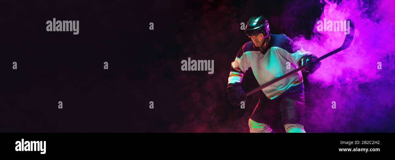 Male hockey player with the stick on ice court and dark neon colored ...