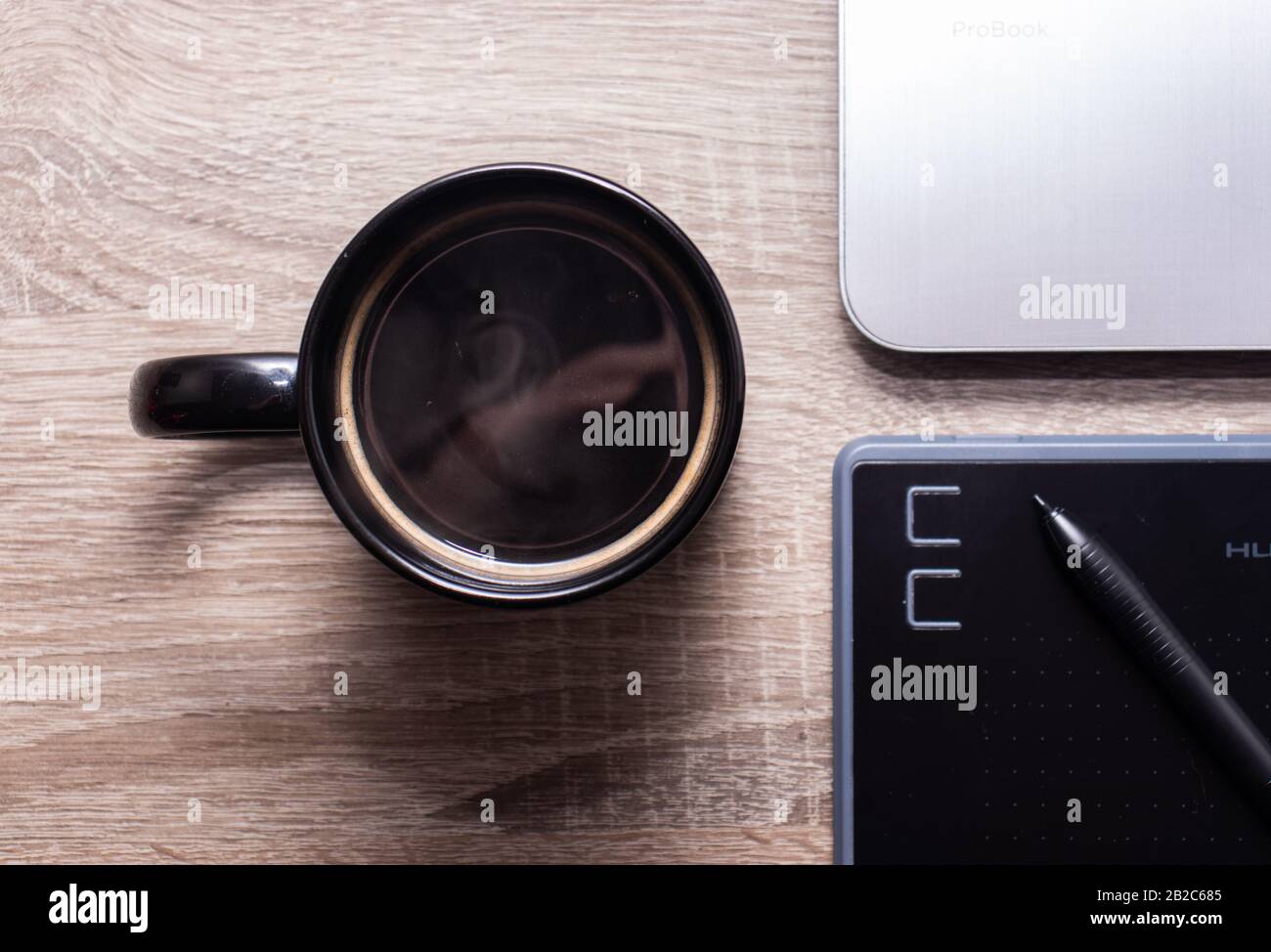 Top down view of a black coffee mug with cofee , edge of laptop and ...
