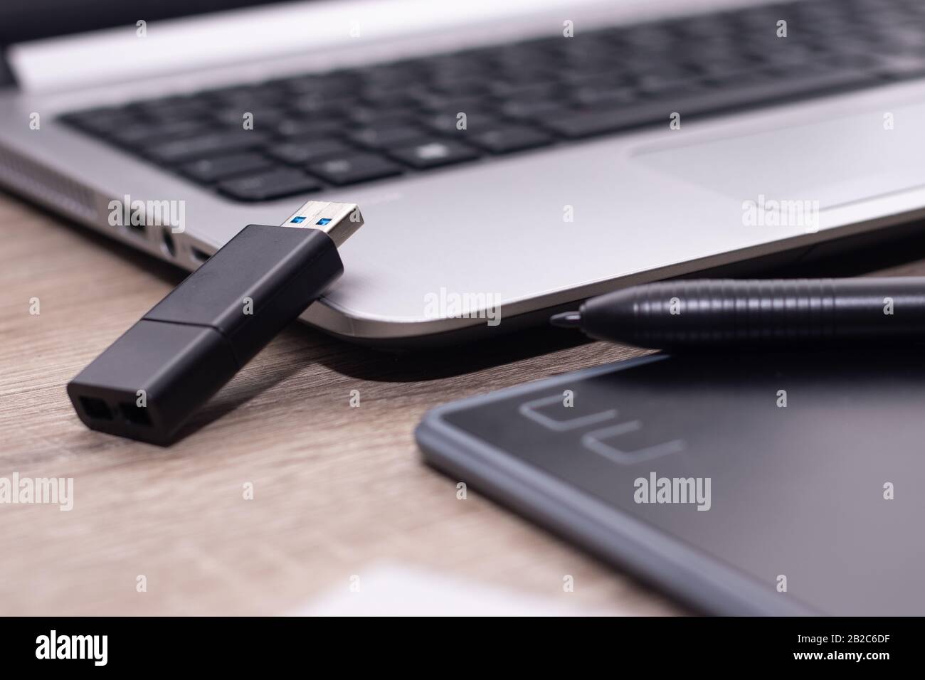 Black graphics tablet surface in front of a silver laptop. Usb drive ...