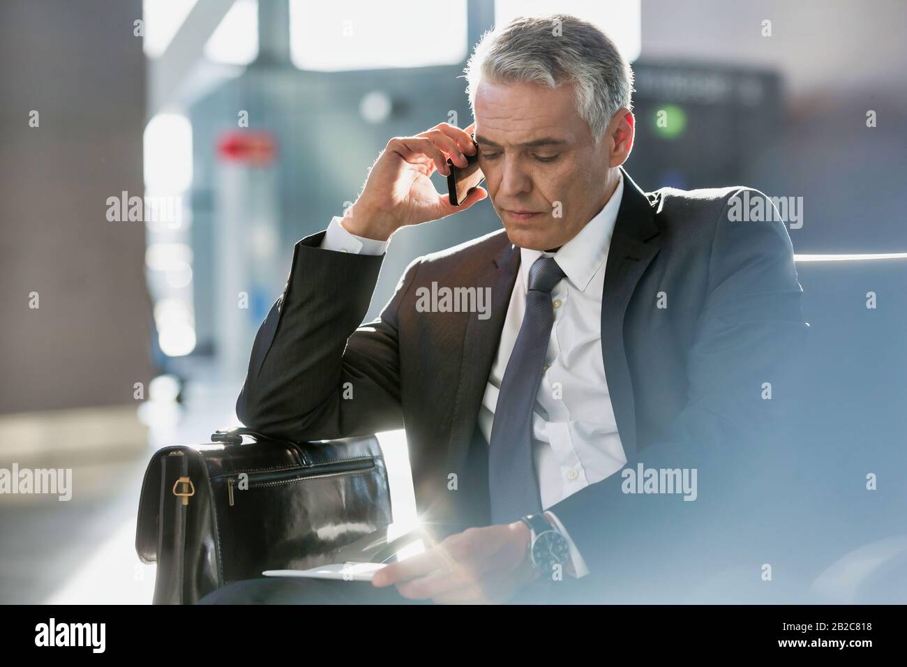 Businessman talking on smartphone while sitting and waiting in his gate ...