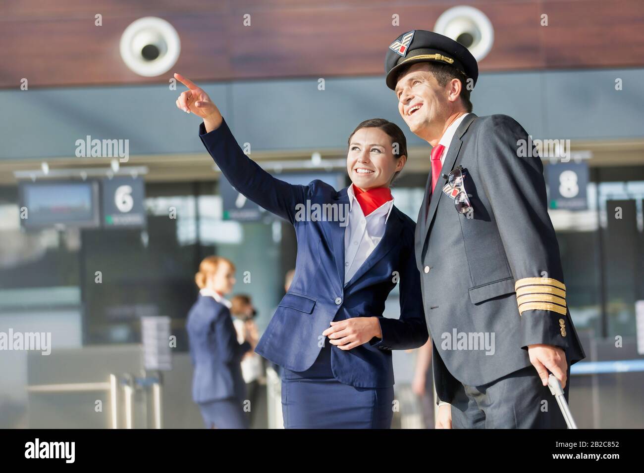 Young attractive stewardess pointing aircraft with the pilot in airport ...