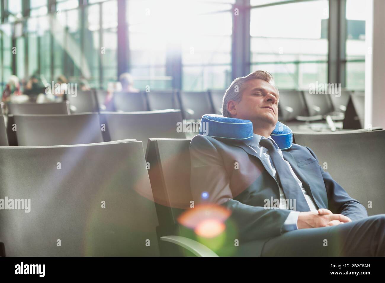 Mature businessman sitting and sleeping with his pillow while waiting for boarding in airport ...