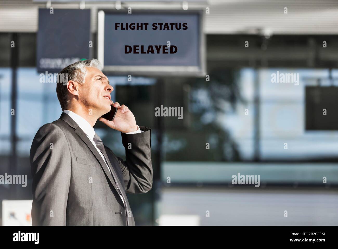 Mature businessman making report on his delayed flight while standing at his boarding gate in ...