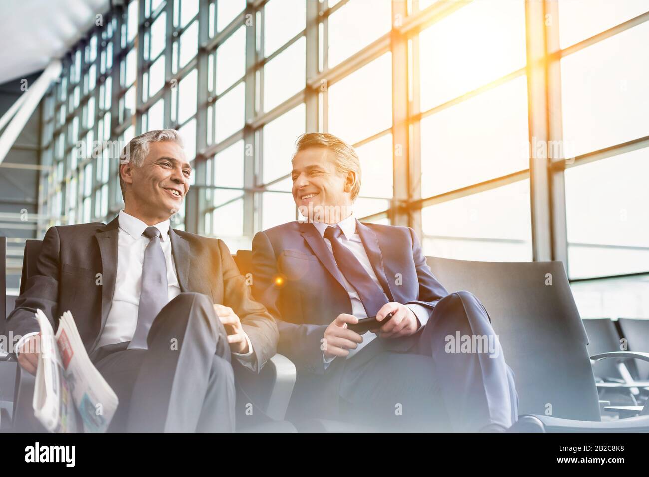 Mature businessmen talking while sitting and waiting for boarding in airport Stock Photo - Alamy