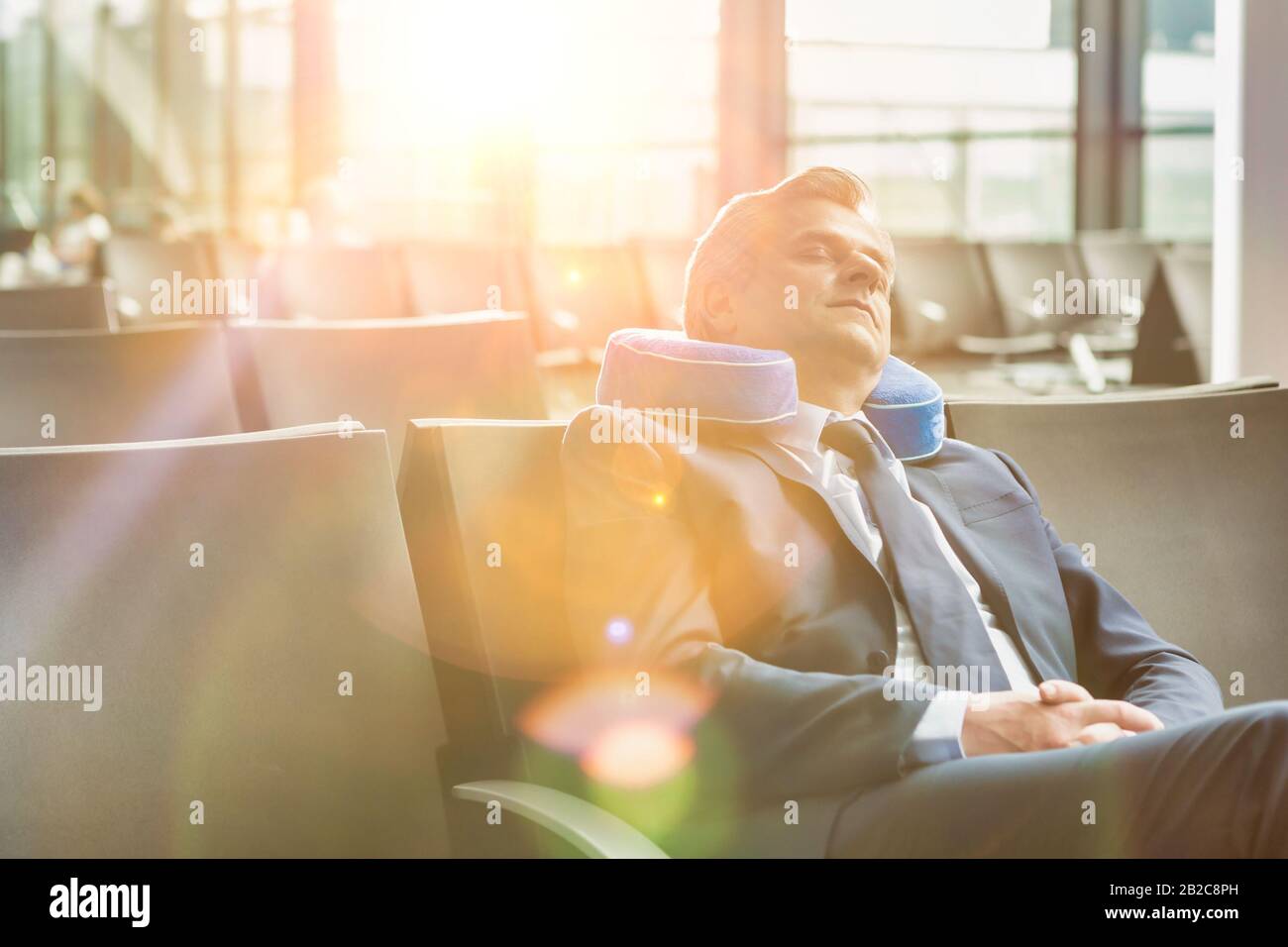 Mature businessman sitting and sleeping with his pillow while waiting for boarding in airport ...
